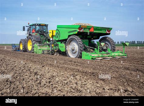 A Farmer Using A Tractor And Planting Implement Plants Potatoes In The