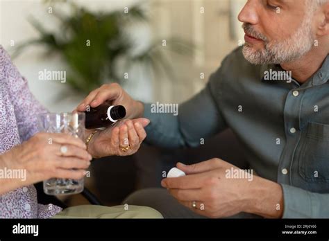 Adult Son Giving Pills To His Ill Mother Helping To Take Medication