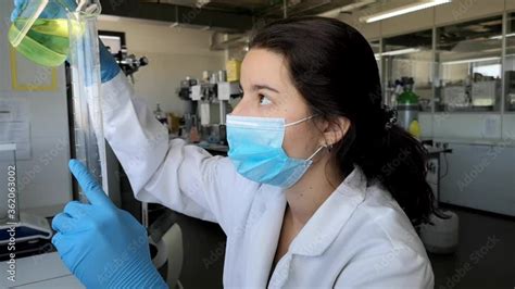 Babe Female Lab Technician Making Up To Volume With Yellow Liquid Into A Measuring Cylinder