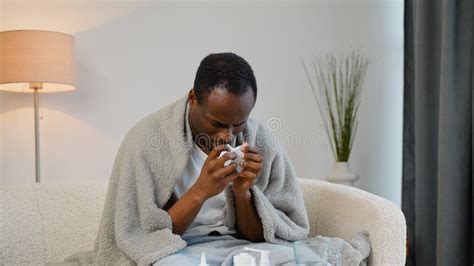 African Man With Runny Nose Sits On The Couch At Home Under A Plaid