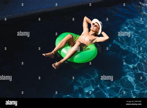 A Young Asian Man Relaxes On A Green Float In A Pool Wearing A White