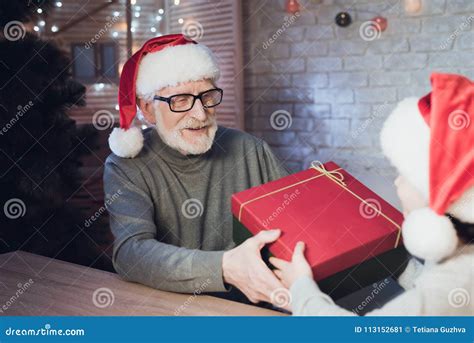 Grandfather And Grandson In Santa Claus S Hats At Night At Home Granddad Is Giving Boy Present