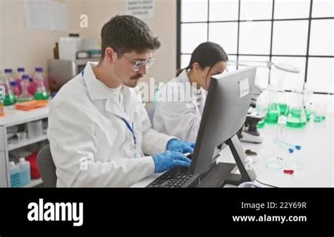 A Man And Woman Scientists In Lab Coats Analyzing Data On A Computer In