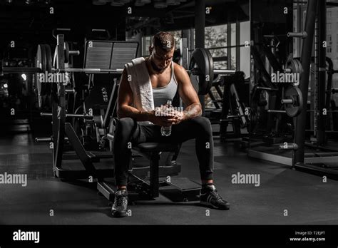 Bearded Man Bodybuilder Sitting On Bench At Gym With Towel Holding