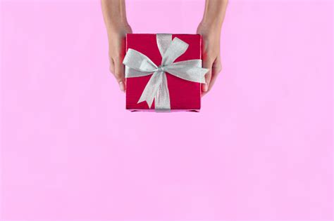 분홍색 배경에 리본이 달린 빨간 종이에 싸여 있는 선물 상자를 들고 있는 여성의 손 맨 위 보기입니다 텍스트공간을 복사합니다 휴일 개념 개념에 대한 스톡 사진 및 기타