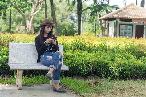 아름 다운 아시아 여자 나무의 자에 앉아 사용 하 여 전화 사업가 나무 벤치 꽃 정원에서 온라인 쇼핑에 앉아 텍스트에 대 한