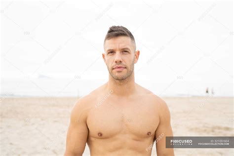 Atleta masculino determinado tronco nu muscular em pé na praia no