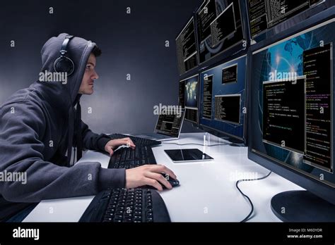Rear View Of A Hacker Using Multiple Computers For Stealing Data In