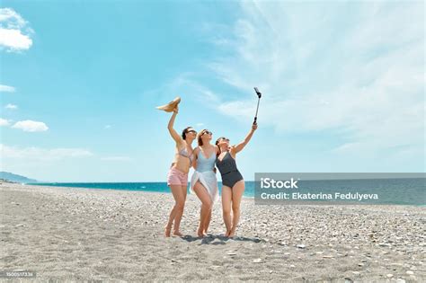 세 명의 여자 친구들이 해변을 걷고 셀카를 찍고 여름날 웃고 있다 쾌활한 여성들이 바다 근처에서 함께 여름 휴가를 즐기고 있다
