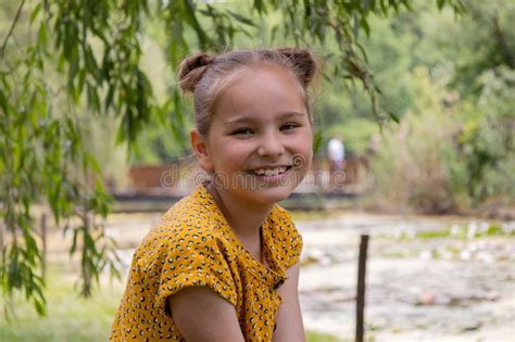 Lovely Small Girl Sitting On A Bench In The Park And Smiling At Camera