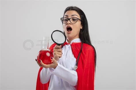 超级英雄高清图片 令人印象深刻的年轻白人超级英雄女孩戴着眼镜和听诊器拿着和看着化学烧瓶与放大镜隔离在白色背景与复制空间 产品实拍免费下载