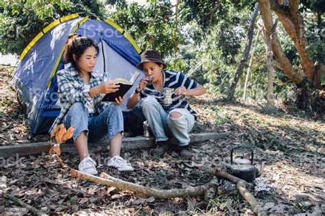 앉아있는 젊은이와 여성은 텐트 밖에 서 책을 읽고 차를 마시는 것입니다 숲에서 우정 캠핑 가죽에 대한 스톡 사진 및 기타 이미지