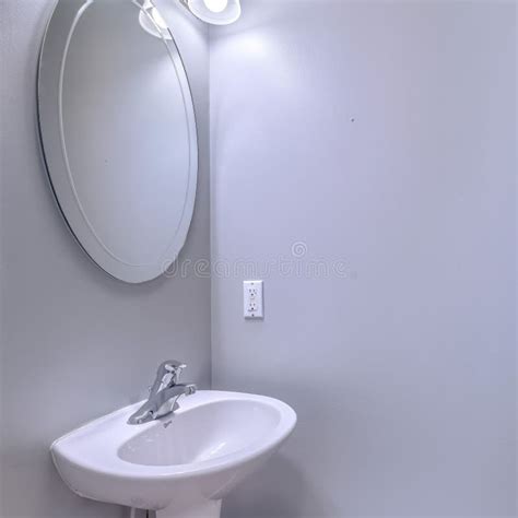 Square Bathroom Interior With Wall Light And Oval Mirror Over Stand