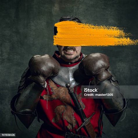 삽화 중세 전사로서의 젊은 남자 어두운 빈티지 배경에 고립 된 기사 그의 얼굴에 노란색 페인트의 무작위 스트로크 예술 창의력 시대 비교 개념 30 34세에 대한 스톡 사진