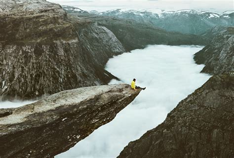 노르웨이 산맥의 트롤퉁가 바위 절벽 가장자리에 남자 여행자 여행 라이프 스타일 모험 감정 개념 극단적 인 휴가 구름 관광 혼자 앉아 위의 야외 가장자리에 대한 스톡 사진 및
