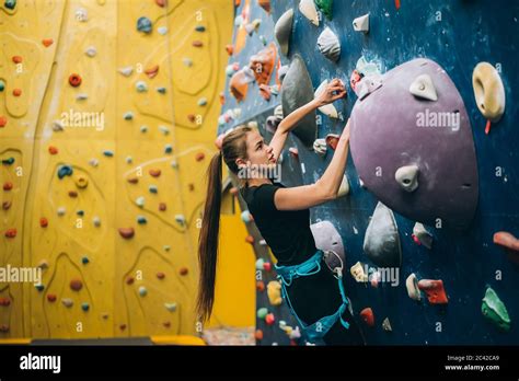 Young Woman Climbing A Tall Indoor Man Made Rock Climbing Wall Stock
