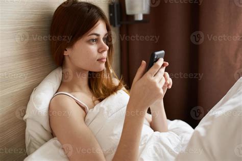 Woman With Mobile Phone Lies In Bed Near Window And Curtains Design
