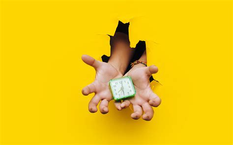 찢어진 노란색 종이 배경을 통해 현대 플라스틱 녹색 알람 시계를 들고 두 남성 손 제 시간에 일어나 여섯 째 아침의 시작 6에