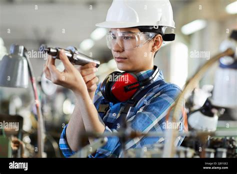 Serious Female Technical Engineer In Construction Hardhat And Safety Goggles Checking Drill Bit