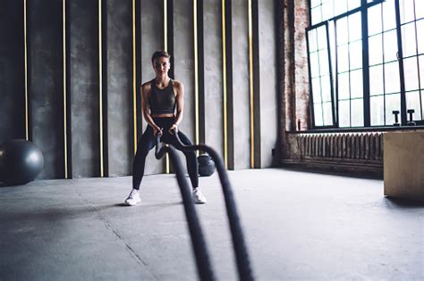 체육관에서 장비로 심장 크로스 핏 훈련을하는 완벽한 인물을 가진 심각한 근육질 여성 슬리밍을 위해 체육관에서 시간을 보내는 파도가있는 활동적인 착용 리프팅 로프에서 슬림 한