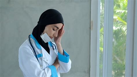 A Muslim Woman Doctor Stands By A Window In The Office Removes The