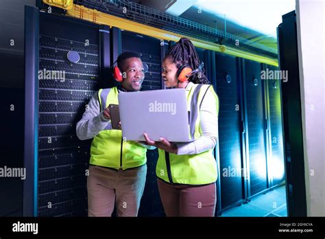 African American Computer Technicians Wearing Headphones Using Laptop Working In Server Room