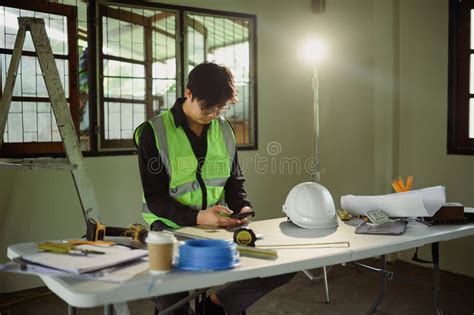 Engineer Checking Phone While Seated At Construction Planning Desk With
