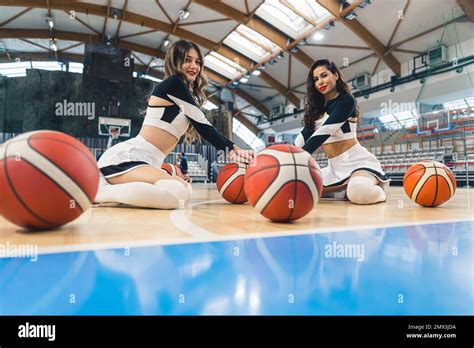 Low Angle Shot Of Two Cheerleaders Sitting With Basketballs On The