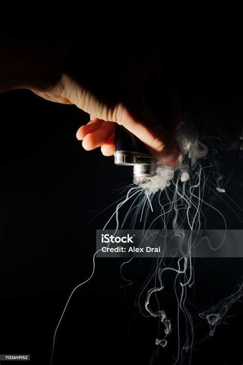 남성 손은 Vape 거꾸로 유지 Vape 구름 검은 배경에 코일에서 시작 합니다 안개는 흰색입니다 스프레이 끓는 글 리세 린으로