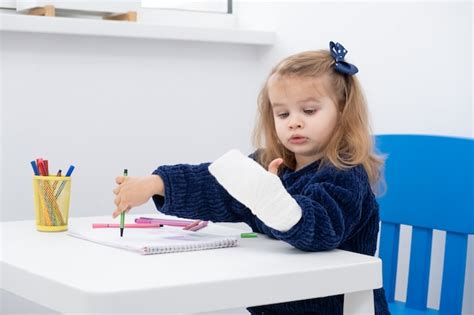 Niña Con Mano Enyesada Sentada En La Mesa Tratando De Dibujar Con