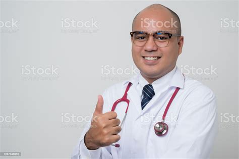 흰색 코트를 입은 의사 청진기는 팔을 건너 엄지 손가락을 위로 쳐다보며흰색 배경에 고립 된 모서리 옆에 미소를 지으며
