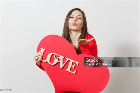 빨간색 캐주얼 옷에 젊은 여자 공기 키스를 보냅니다 그리고 큰 레드 심장 흰색 배경에 나무 말씀 사랑을 보유 하 고 있습니다 광고에 대 한 공간을 복사 합니다 성 발렌타인의