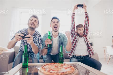 미친 재미 기쁨 승자와 패자 젊은 남자는 소파에 앉아와 비디오 게임 가정 실내에서 맥주와 피자 감정과 감정 표현 몸짓 Brand