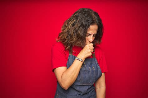 빨간 고립된 배경 위에 앞치마 유니폼을 입은 중년 노인 여성은 감기 나 기관지염의 증상으로 기분이 좋지 않고 기침합니다 헬스케어