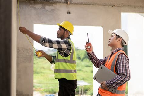 안전모를 쓴 감독 엔지니어 또는 건축가가 노트북과 청사진을 들고 미완성 건물의 건설 구역에서 부동산 건설에 대한 세부 사항을 확인합니다 2명에 대한 스톡 사진 및 기타