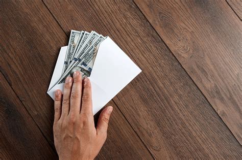 남자의 손 그리고 Dolors 흰 봉투 나무 테이블에 상단 보기에에서 미국의 소득 상 여 또는 뇌물의 개념입니다 부패 급여