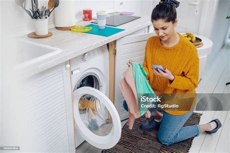행복한 젊은 여자 준비 그녀의 세탁 용 세척 및 스마트폰 사용 세탁기에 대한 스톡 사진 및 기타 이미지 세탁기 젊은 여자 20 24세 Istock