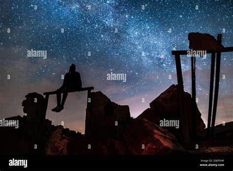 Silueta de una persona sentada en una tabla bajo un cielo estrellado por la noche Fotografía de