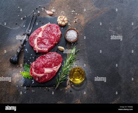 Raw Ribeye Steak Or Beef Steak On The Graphite Cutting Board With Herbs