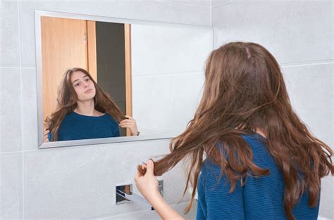 아름 다운 십 대 소녀 거울 전에 그녀의 머리를 하 고 화장실에서 서 서 거울에 있는 그녀의 반영을 보고 거울에 대한 스톡 사진