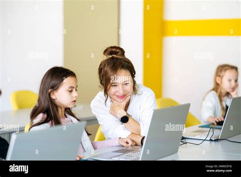 Smiling Teacher Teaching Computer Coding On Laptop To Girl In Classroom