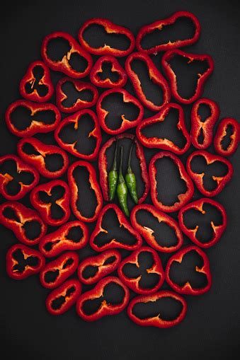 어두운 배경에 신선한 녹색 고추를 둘러싸고 있는 생생한 빨간 피망 조각의 예술적 배열은 대담한 색상 자연스러운 질감 및 요리 창의성을 보여줍니다 0명에 대한 스톡 사진 및