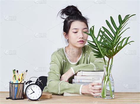 学生女孩坐在书桌前，桌上放着一堆书和闹钟，一杯牛奶放在白色的背景上。