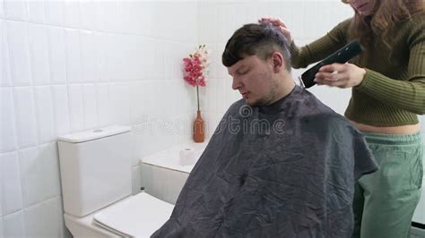 Young Caucasian Woman Cutting Man Hair In Bathroom At Home Stock