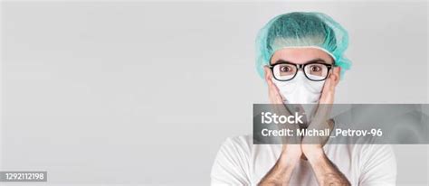 흰색 의료 마스크와 의료 모자를 쓴 의사 외과 의사는 손으로 얼굴을 잡고 놀랍게도 흰색 배경 위에 서 있습니다 대구 19 독감 및 계절감기의 Doncept 19에 대한 스톡