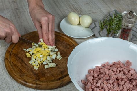 주부는 고기 샐러드를 만들기 위해 나무 도마에 삶은 달걀을 잘게 자릅니다 부엌 칼로 나무 도마에 삶은 달걀을 자르는 여성 손의
