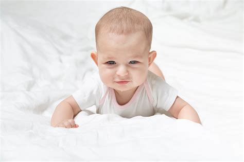 흰 옷의 아기 소녀는 흰 침대에 누워 빈 복사 공간을 보고 있습니다 그녀의 뱃속에 누워 웃는 유아 아이 고리 물리개에 대한 스톡