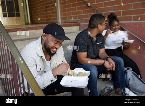 Happy Young Man Eating Takeout Food With Friends On Urban Steps Stock