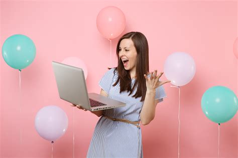 블루 드레스를 입고 화려한 공기 풍선 핑크 배경에 손을 확산 노트북 Pc 컴퓨터를 사용 하 여 들고 좋아 라 행복 한 젊은