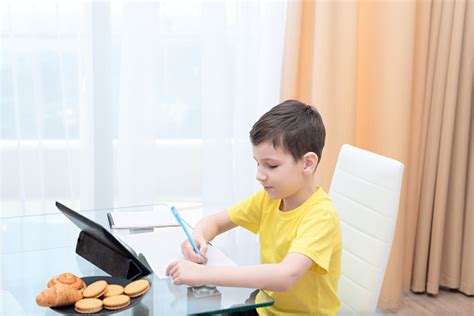 노란색 티셔츠를 입은 소년이 집에서 온라인 학교 수업에 참석하는 디지털 태블릿을 들고 테이블에 앉아 있다 원격 학습 온라인 교육 개념 6 7 살에 대한 스톡 사진 및 기타